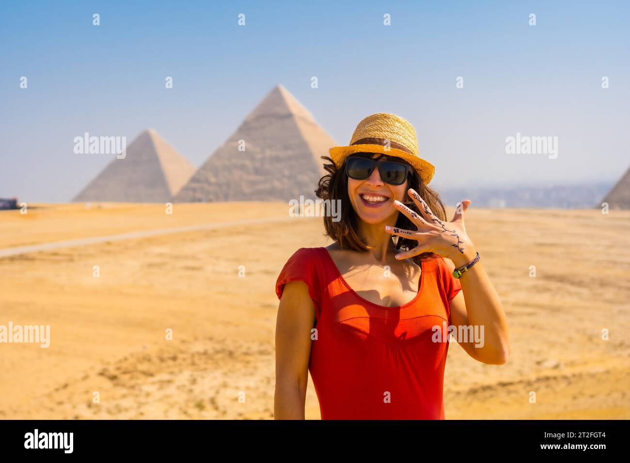 Portrait of a young tourist in red dress enjoying the pyramids of Giza ...