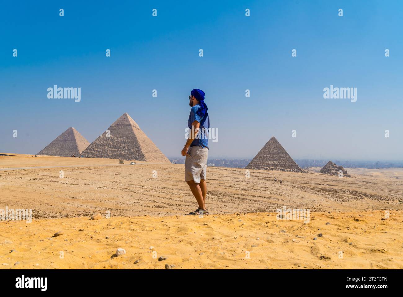 Portrait of a young man in a blue turban walking next to the Pyramids ...