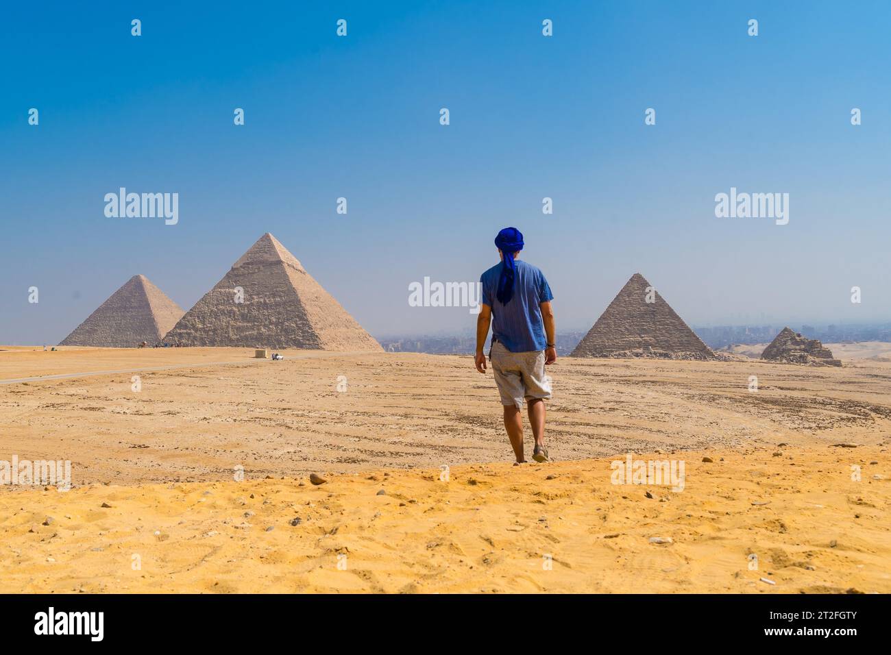 A young man in a blue turban walking next to the Pyramids of Giza, the ...