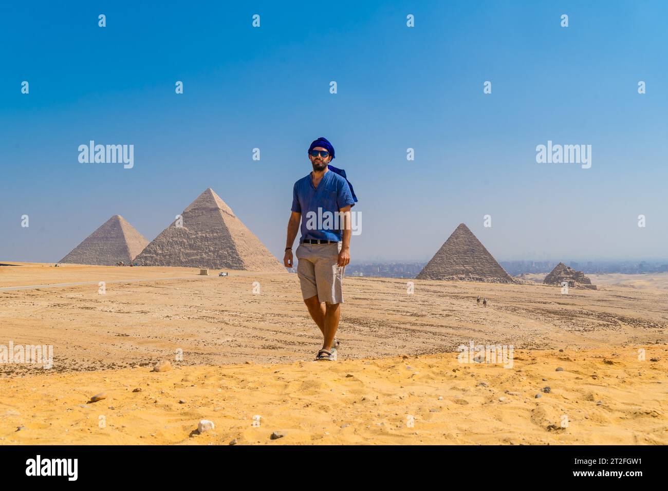 Portrait of a young man in a blue turban walking next to the Pyramids ...