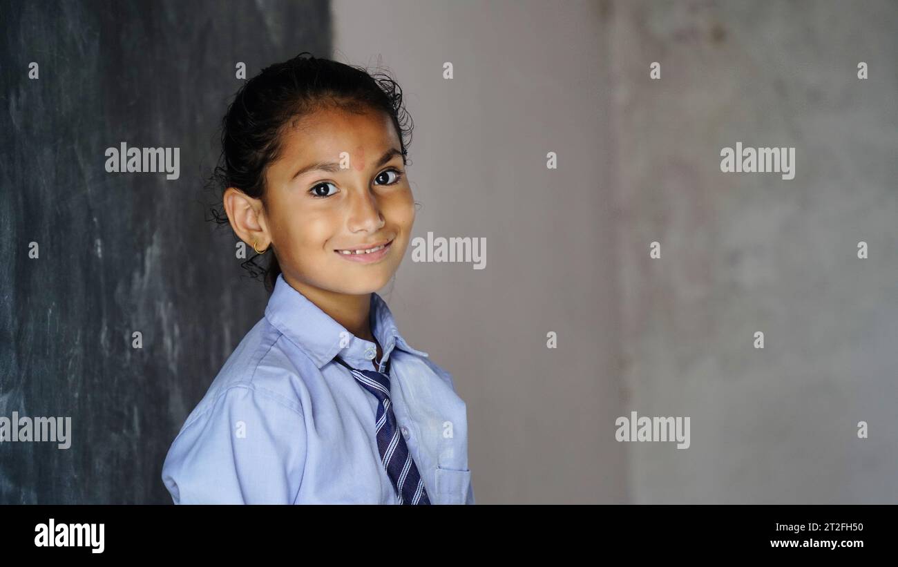 Happy Indian school girl child standing in front of black chalkboard ...