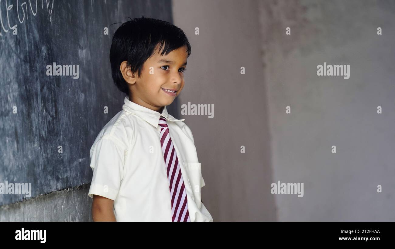 Indian school boy standing against blank chalkboard, intelligent and ...