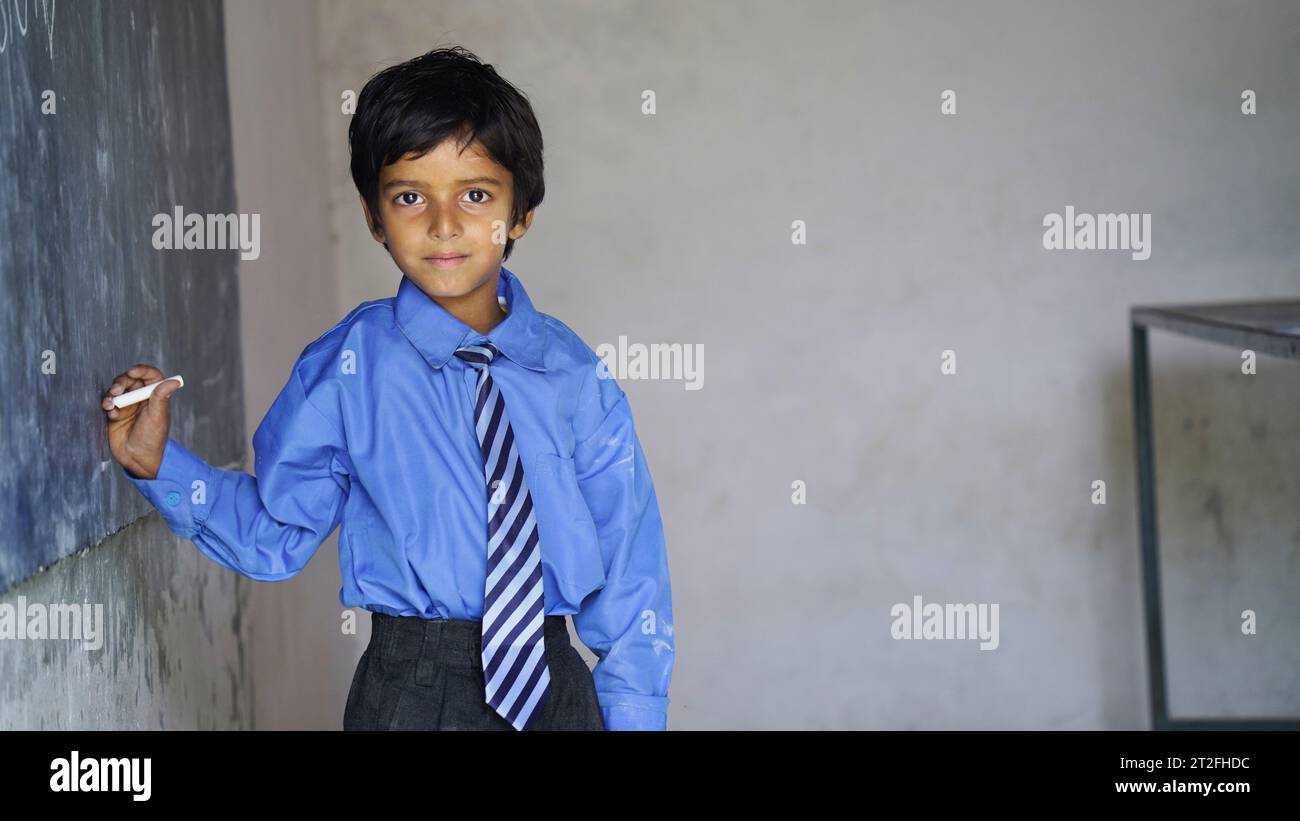 Indian school boy standing against blank chalkboard, intelligent and ...