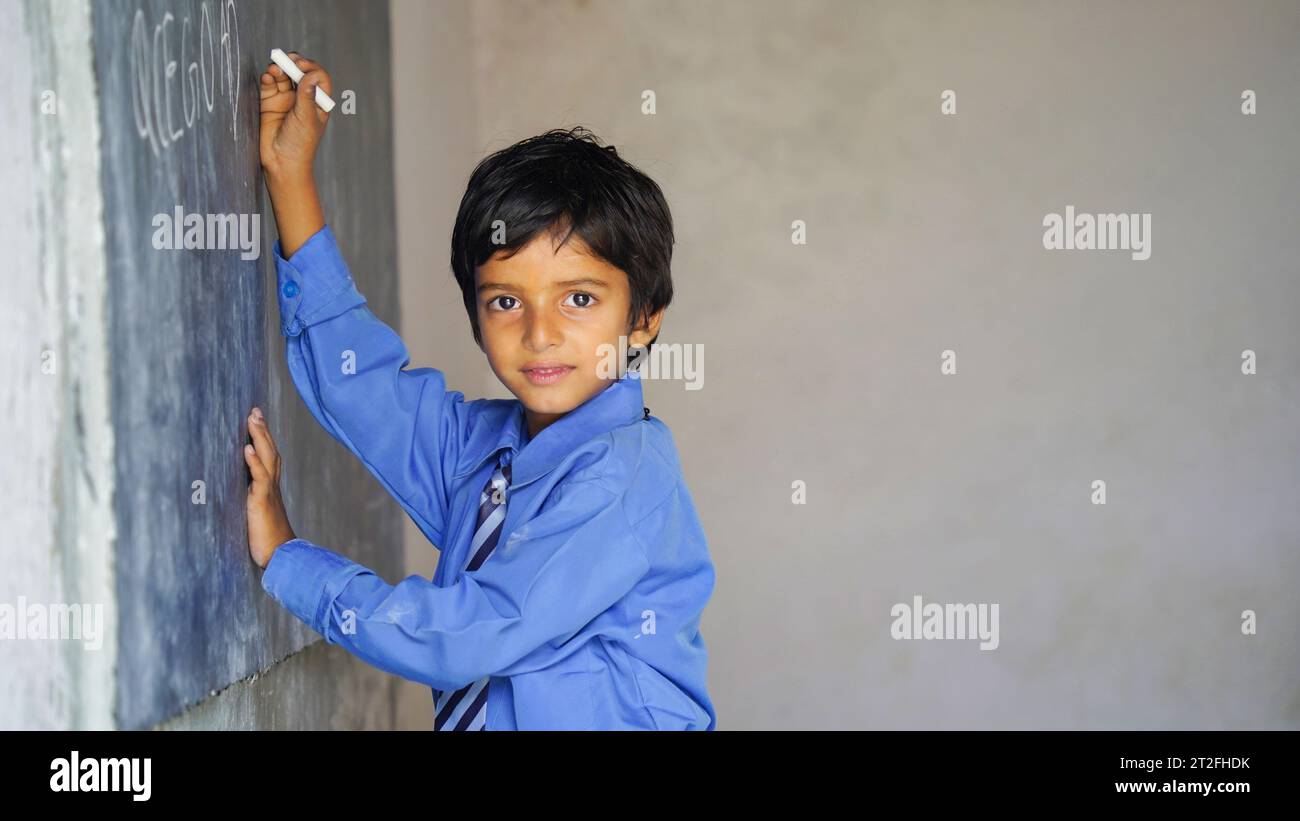 Indian school boy standing against blank chalkboard, intelligent and ...