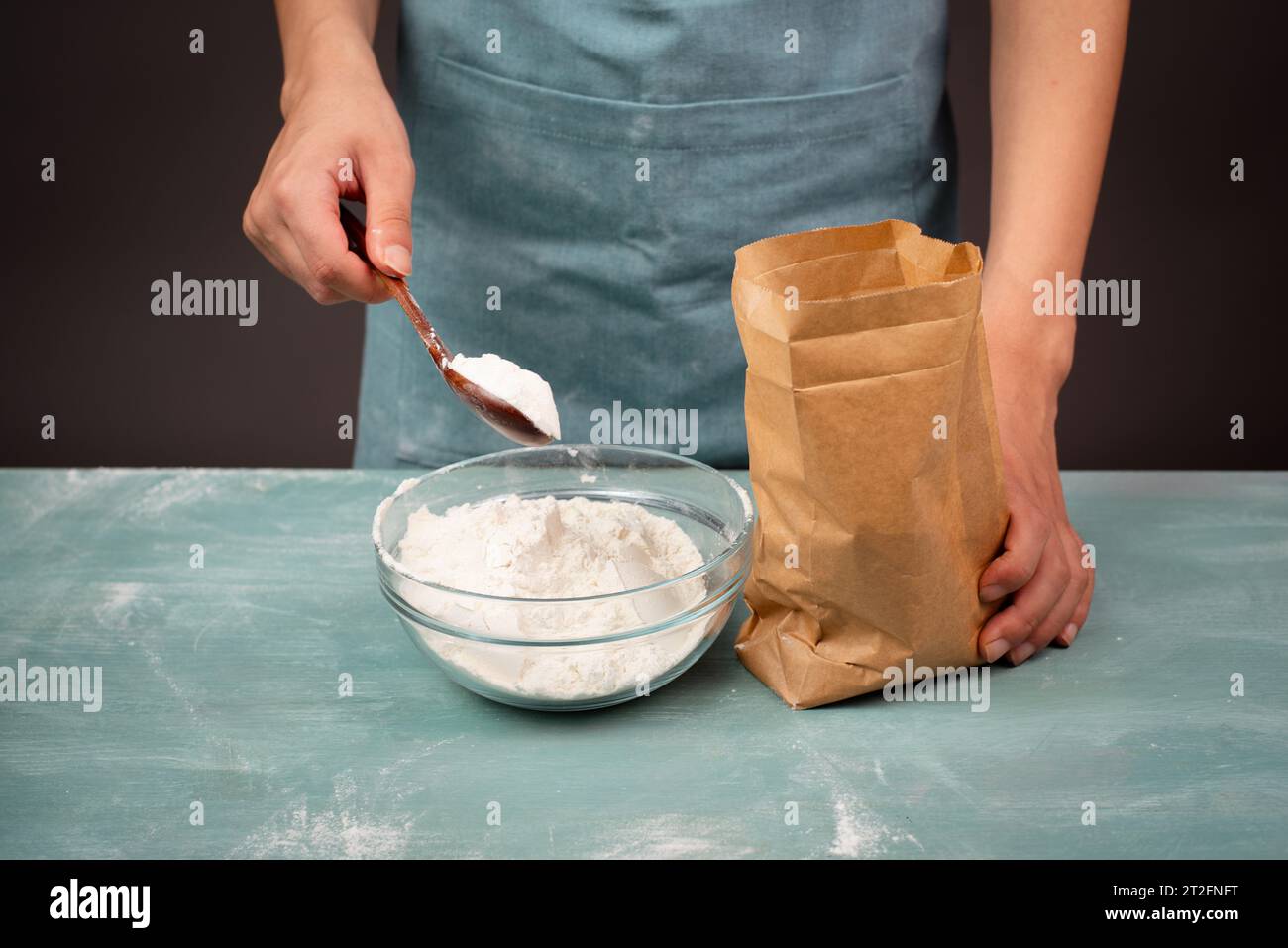 Baker puts wheat flour with a spoon in a bowl, paper bag with baking ...