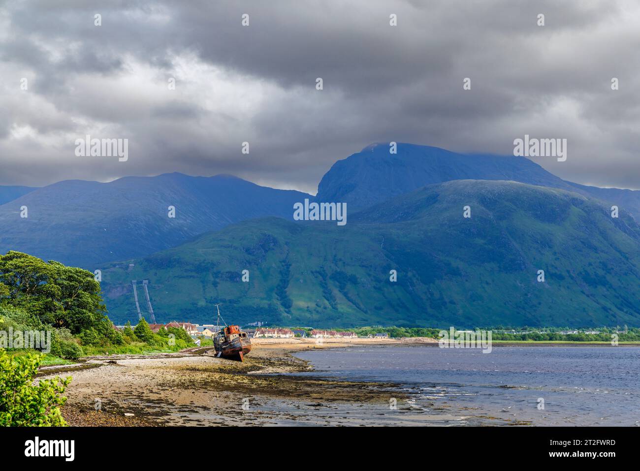 A wrecked fishing boat on the shore of Loch Linnhe, the village of Caol ...