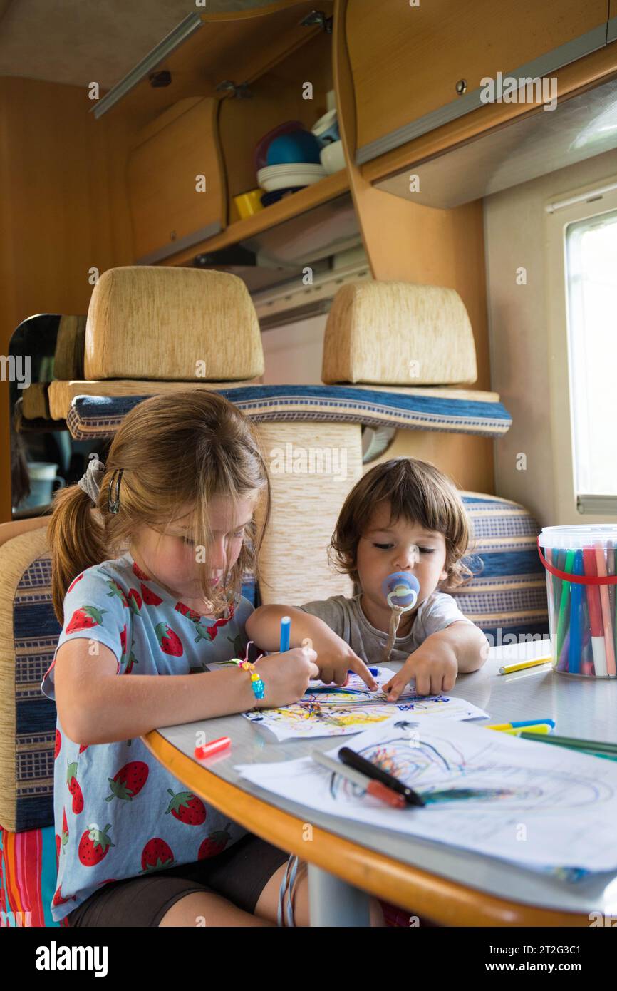 Two caucasian children, brother and sister, drawing on a campervan ...