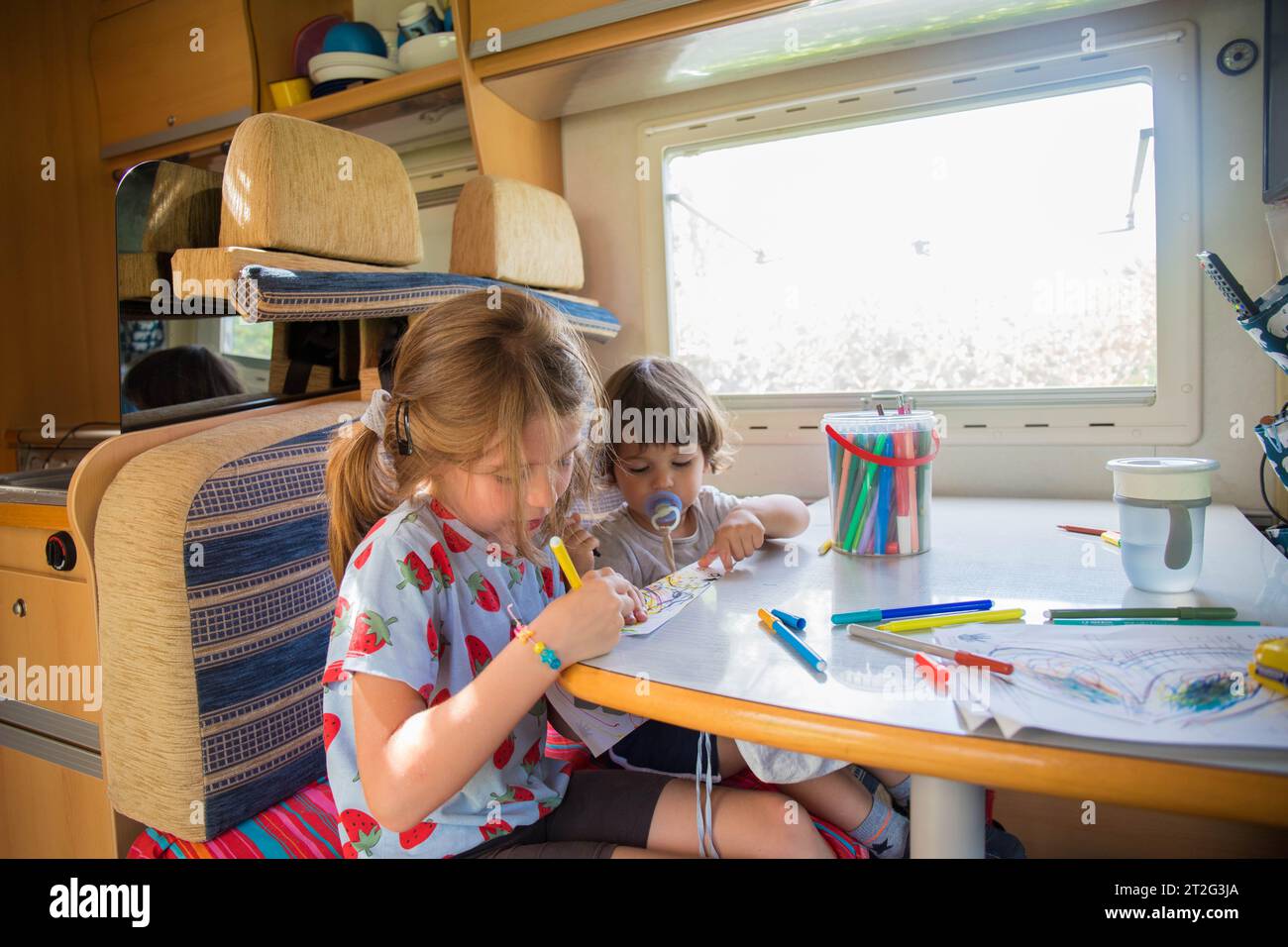 Two caucasian children, brother and sister, drawing on a campervan ...