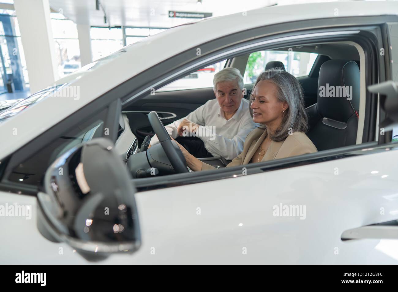 An elderly couple chooses a new car at a car dealership. Mature woman ...