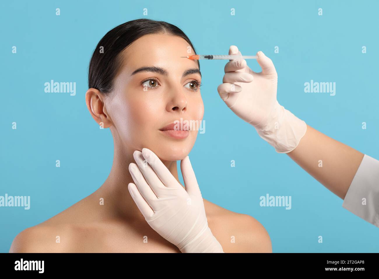 Doctor giving facial injection to young woman on light blue background ...
