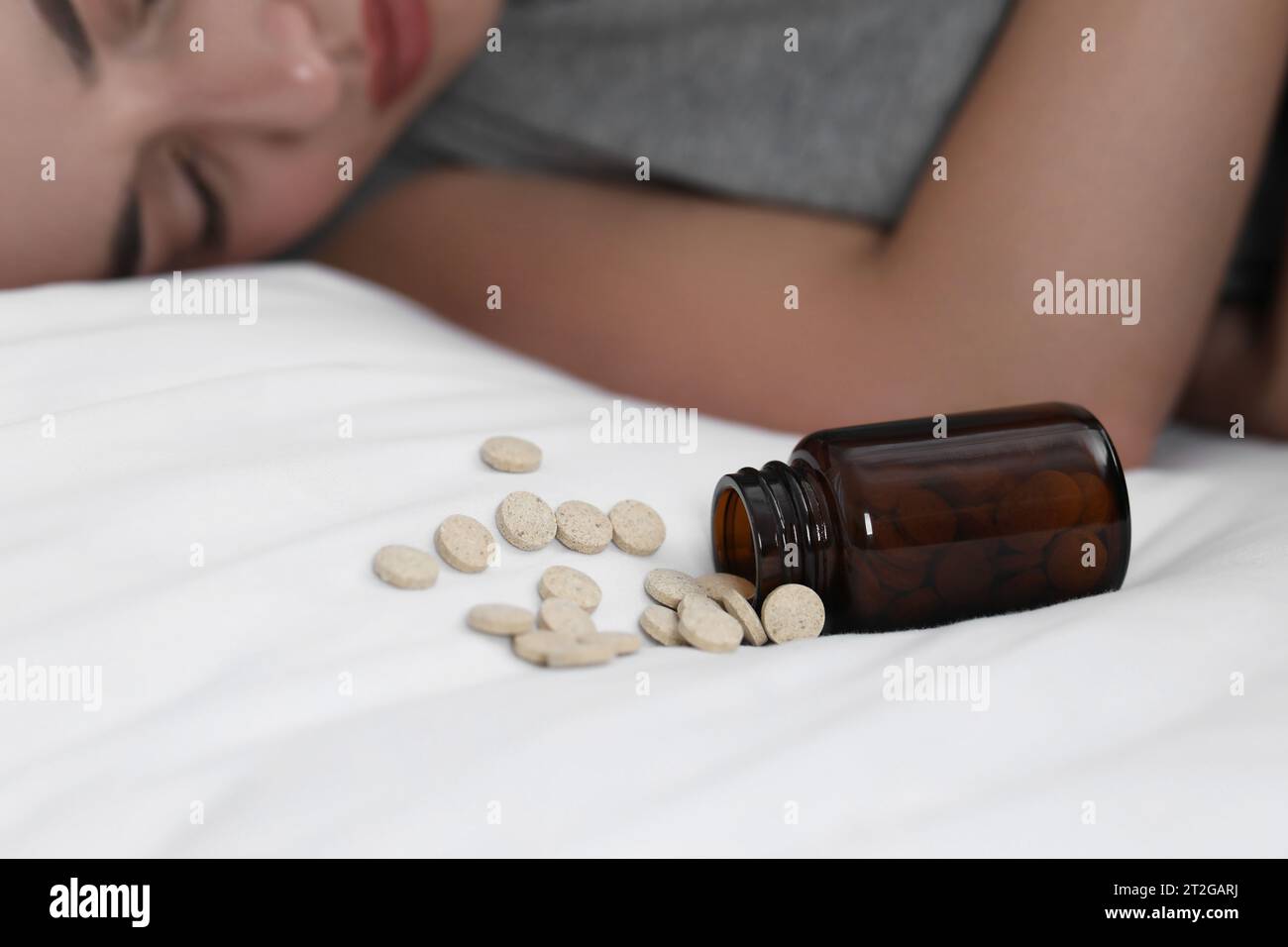 Woman sleeping on bed near overturned bottle with antidepressants ...