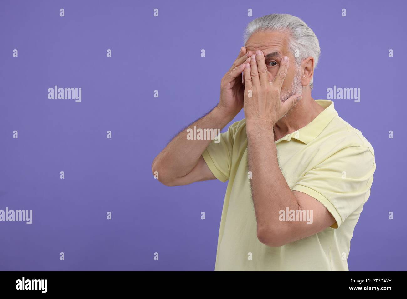 Embarrassed senior man covering face on purple background. Space for ...