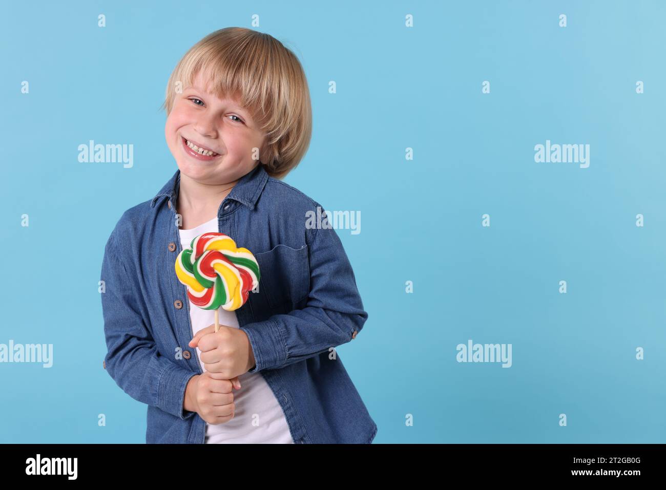 Happy little boy with colorful lollipop swirl on light blue background ...