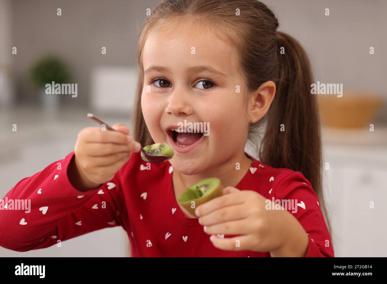 Cute little girl eating fresh kiwi indoors Stock Photo - Alamy