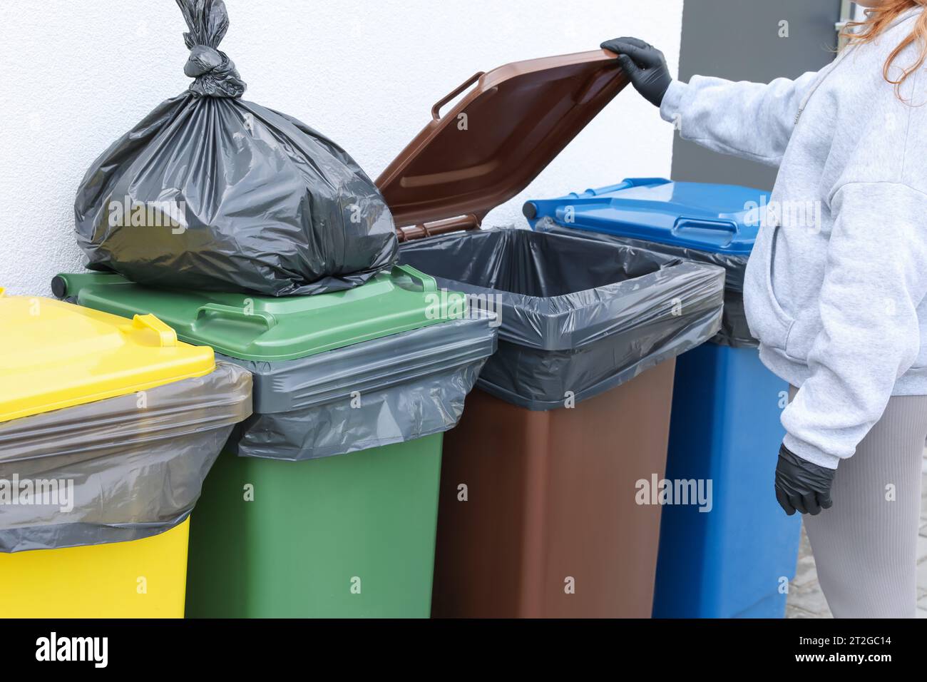 Woman opening bin to throw trash bag full of garbage outdoors, closeup ...
