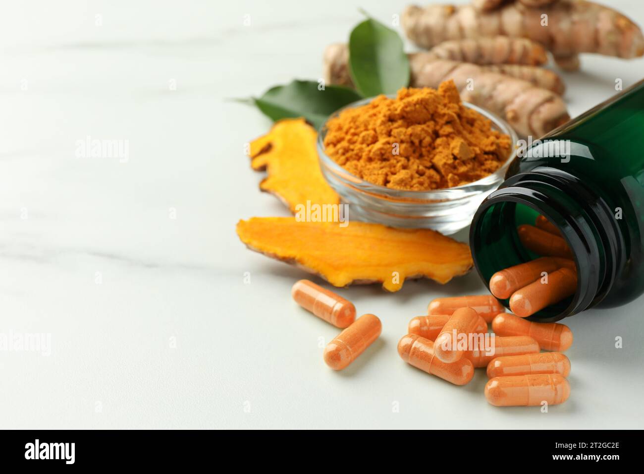 Aromatic turmeric powder, pills and raw roots on white marble table ...
