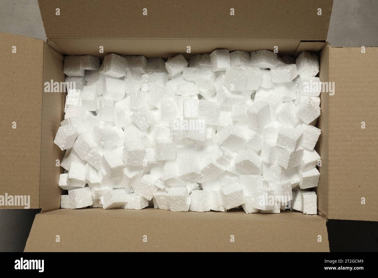 One open cardboard box with pieces of polystyrene foam on grey floor ...