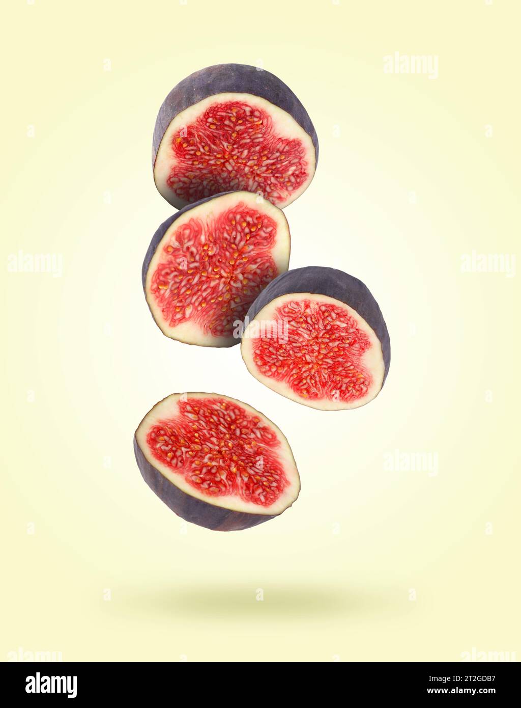 Halved fresh figs falling on pale yellow background Stock Photo - Alamy