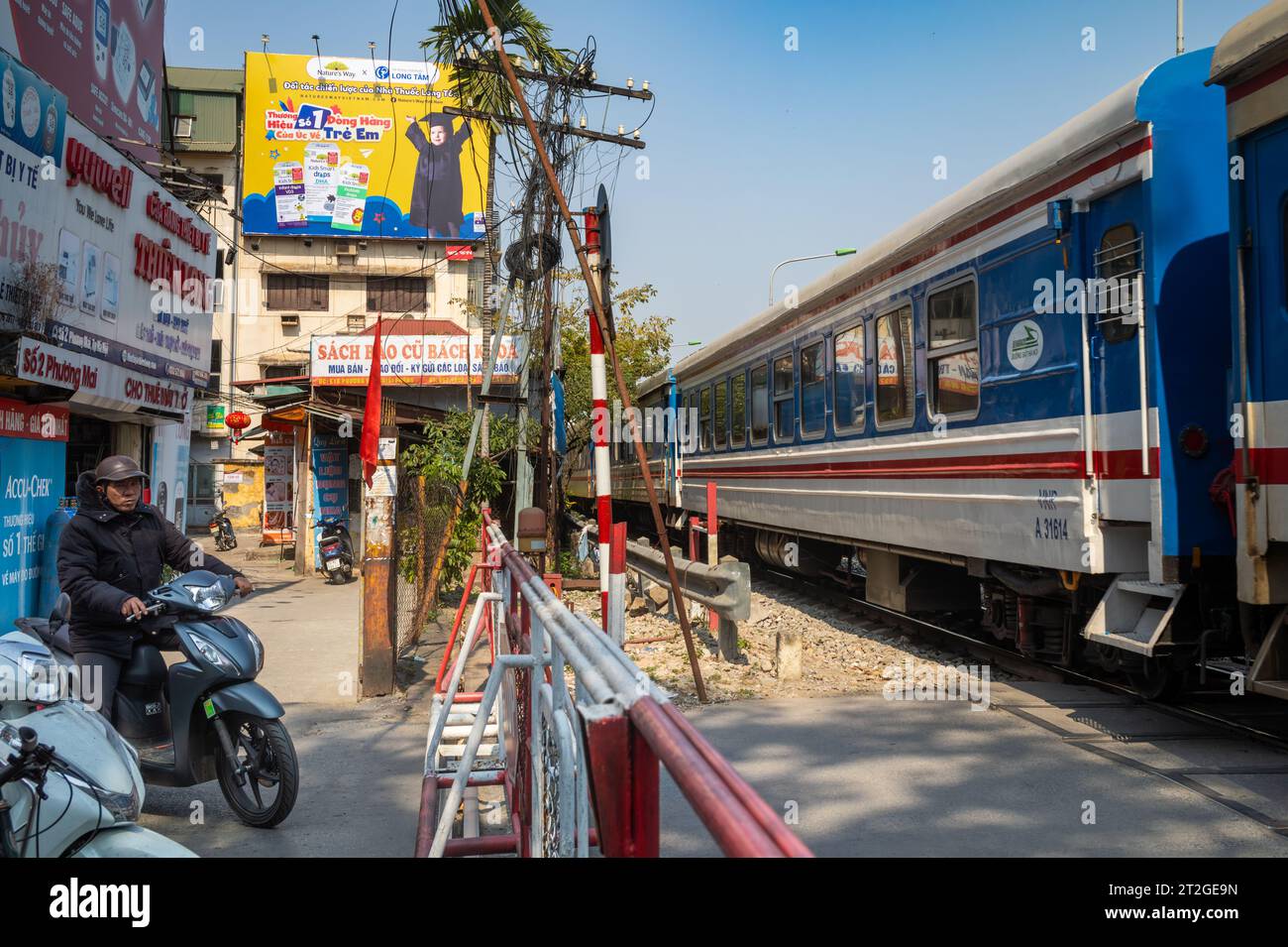 A Vietnam Railways train passes people on motorcycles and bicycles at a ...