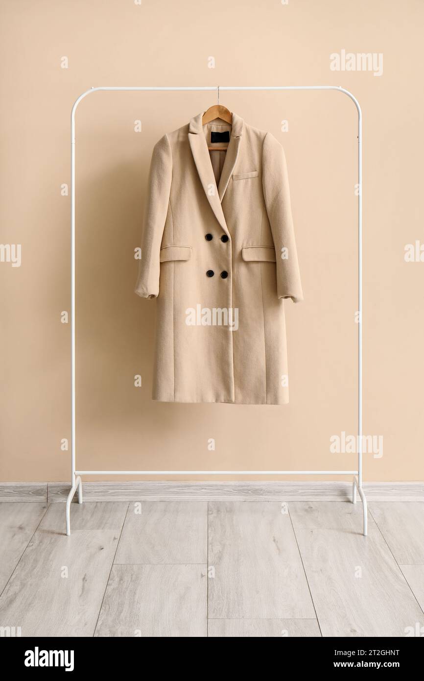 Stylish coat hanging on rack against color wall Stock Photo - Alamy