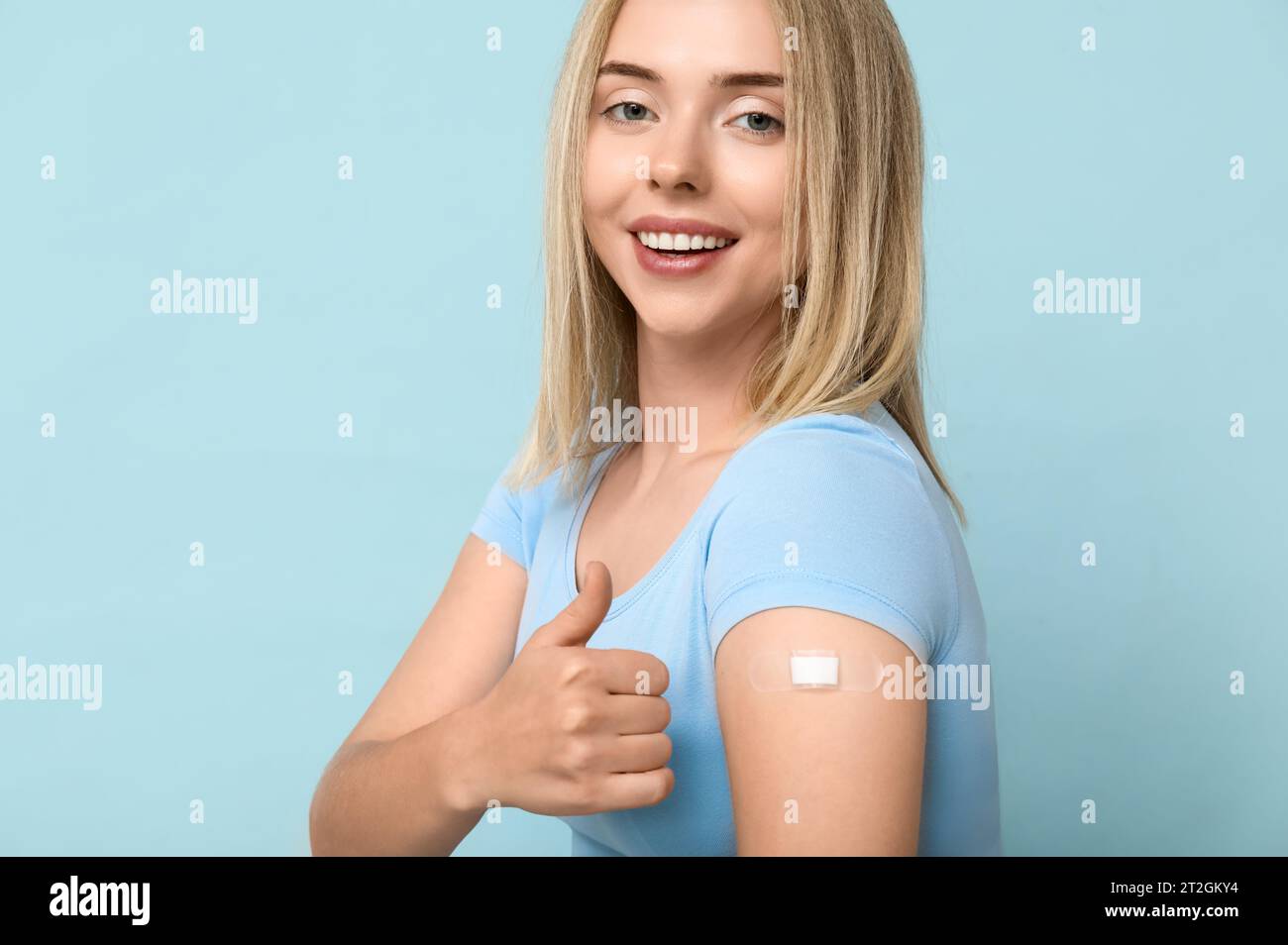 Young woman with medical patch on arm showing thumb-up against blue ...