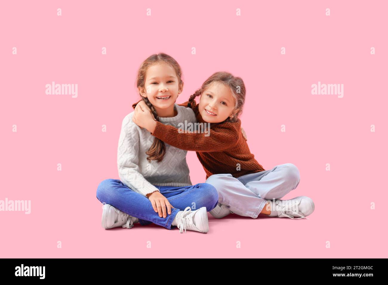 Cute little girls in warm sweaters hugging on pink background Stock ...