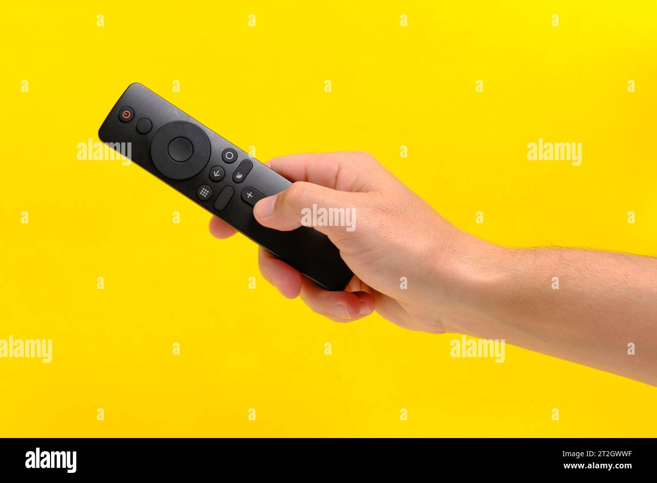 Hand yellow background holds TV remote by pressing button with finger ...
