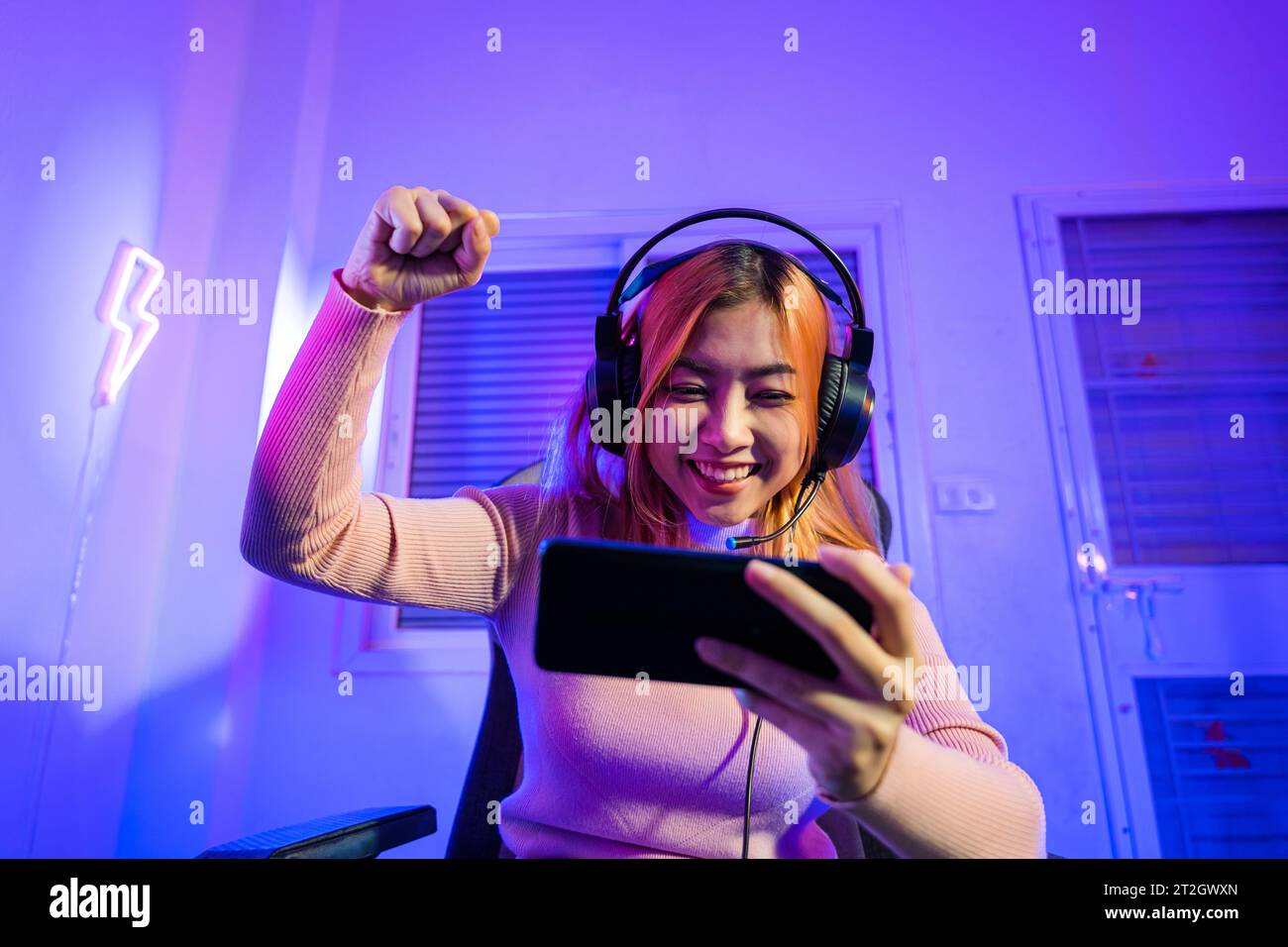 Happy Gamer playing video game online with smartphone she raises hands ...