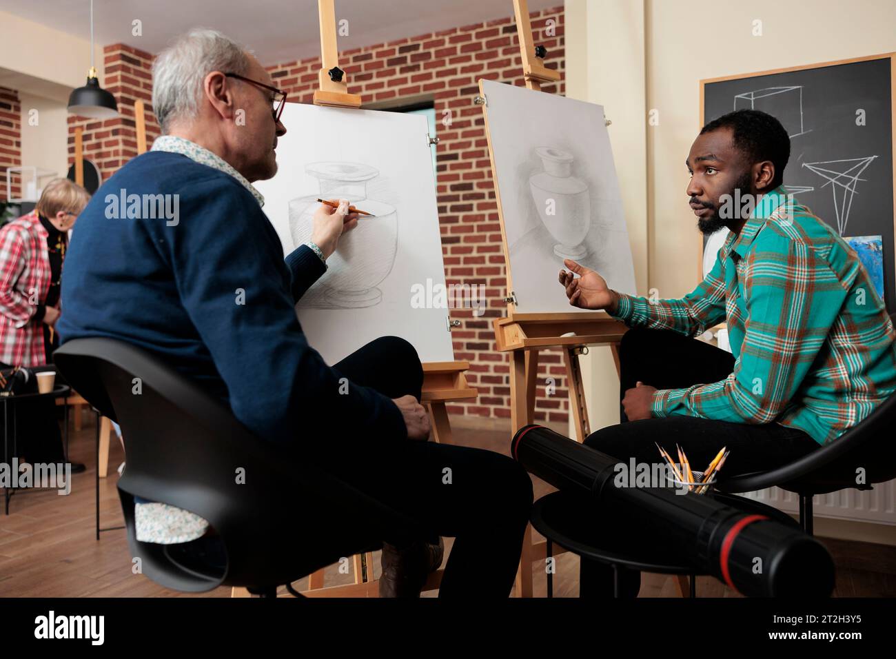 Two diverse men art school students talking during lesson, sitting at ...