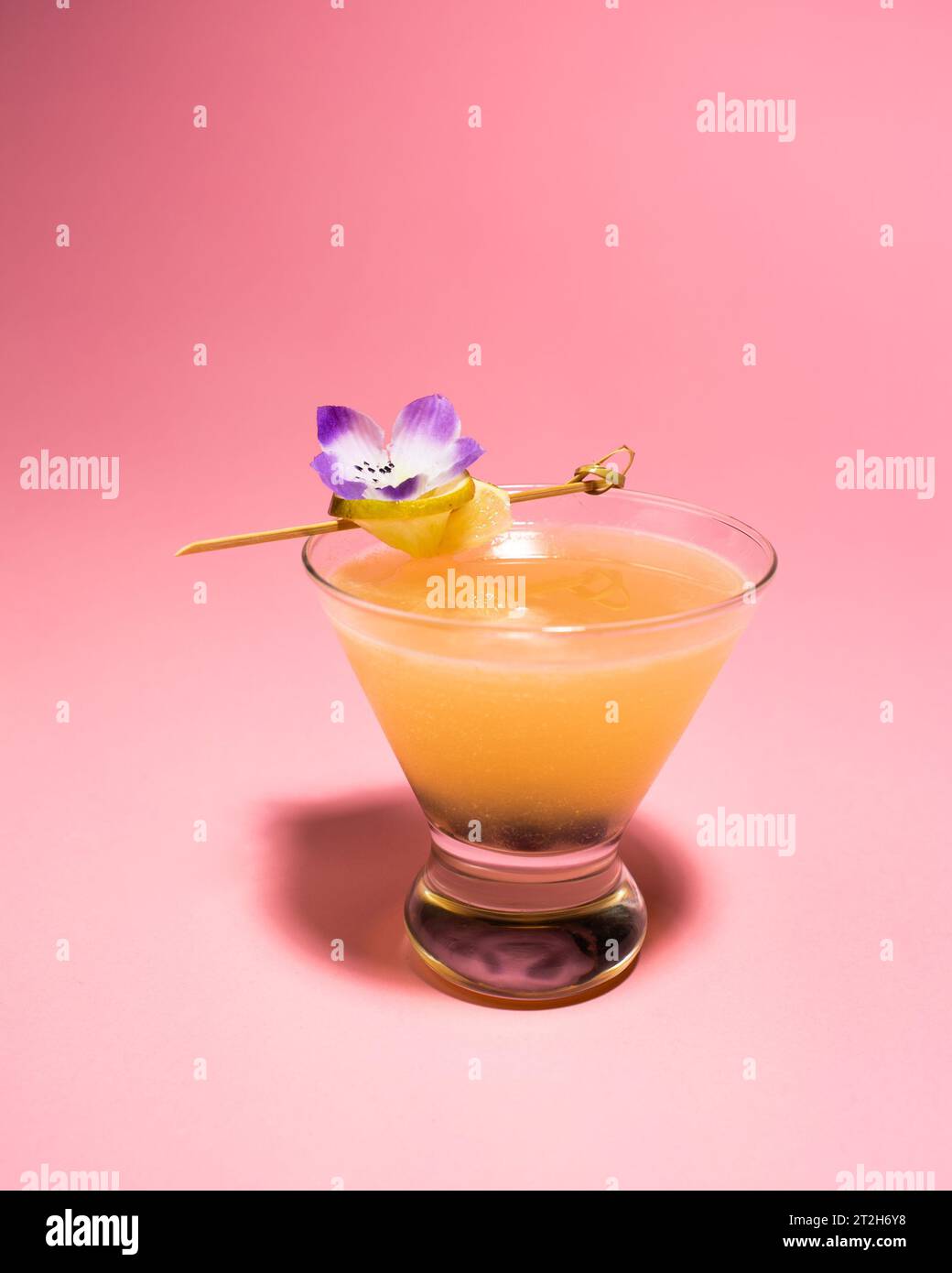 A passionfruit cocktail in a clear glass, garnished with a purple ...