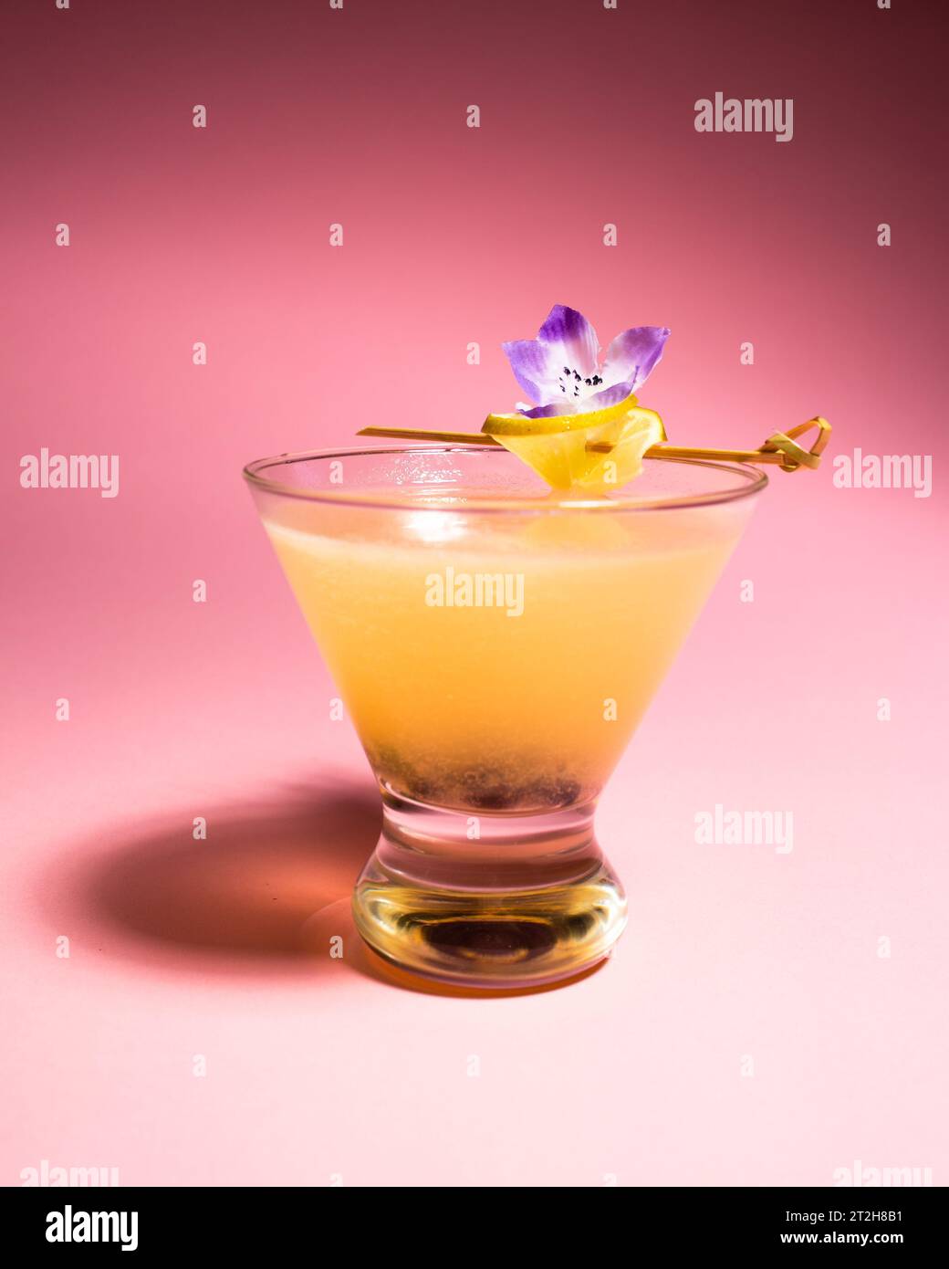A passionfruit cocktail in a clear glass, garnished with a purple ...