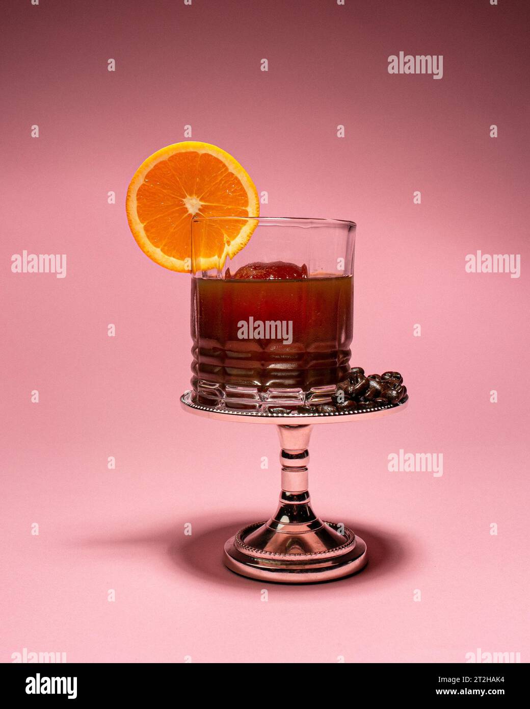 A refreshing cocktail with an orange slice garnish atop a silver stand ...