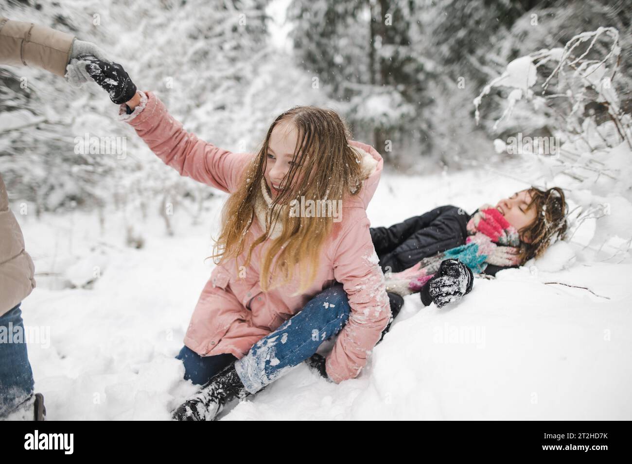 Funny teen sisters and their mother having fun on a walk in snow covered pine forest on chilly ...