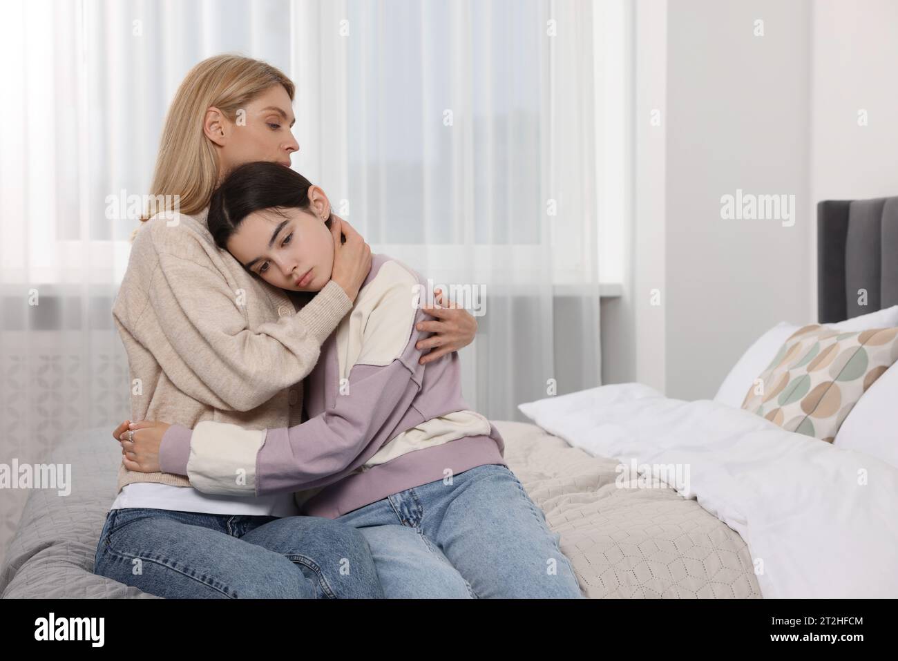 Mother consoling her upset daughter in bedroom, space for text ...
