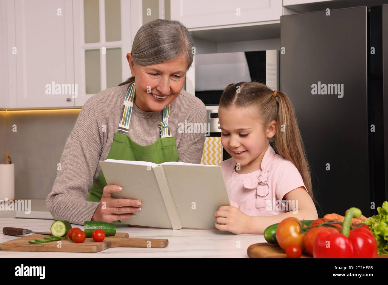 Cute little girl with her granny cooking by recipe book in kitchen ...