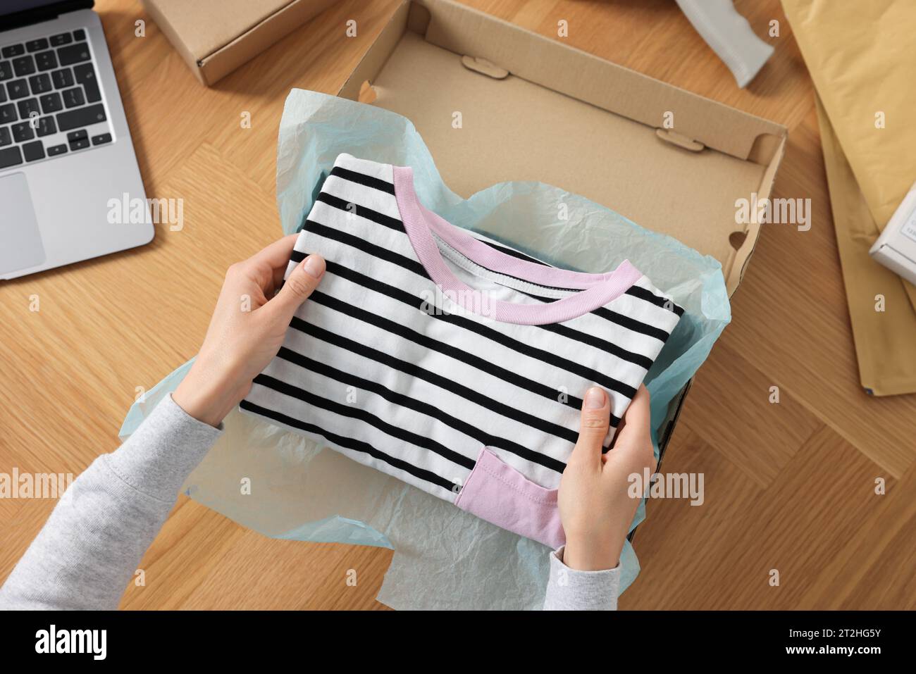 Woman packing clothes into cardboard box at wooden table, top view ...