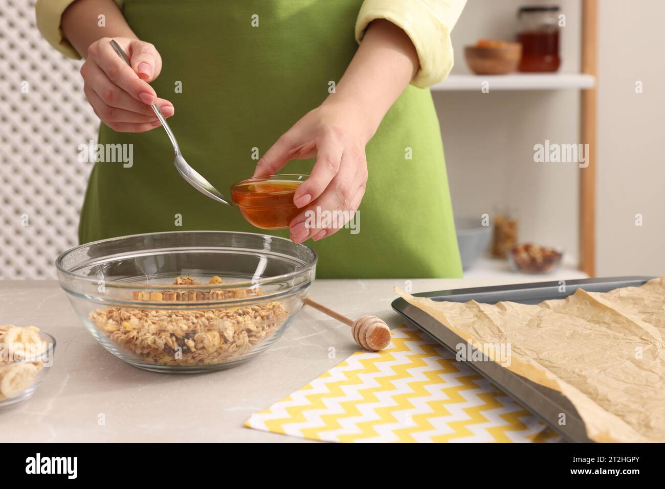 Making granola. Woman adding honey into bowl with mixture of oat flakes ...