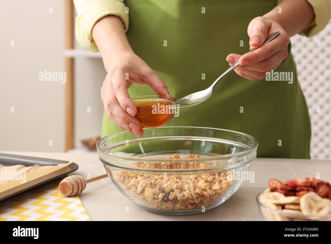 Making granola. Woman adding honey into bowl with mixture of oat flakes ...