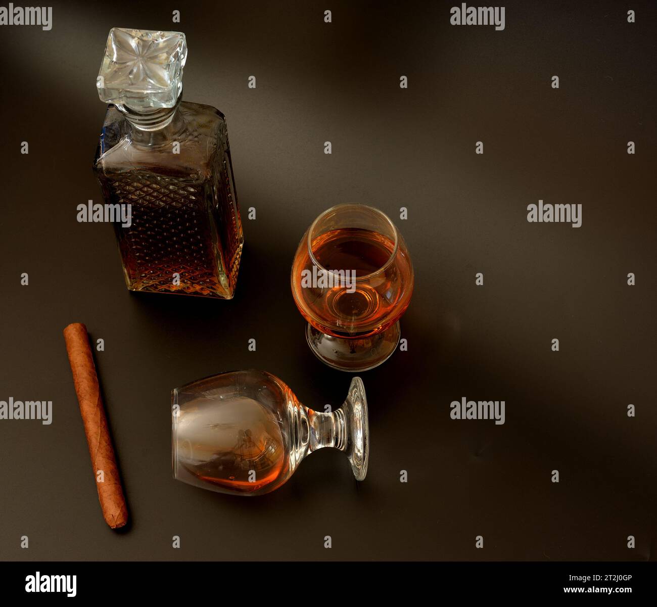 A crystal decanter and two glasses of cognac next to a cigar on a black ...