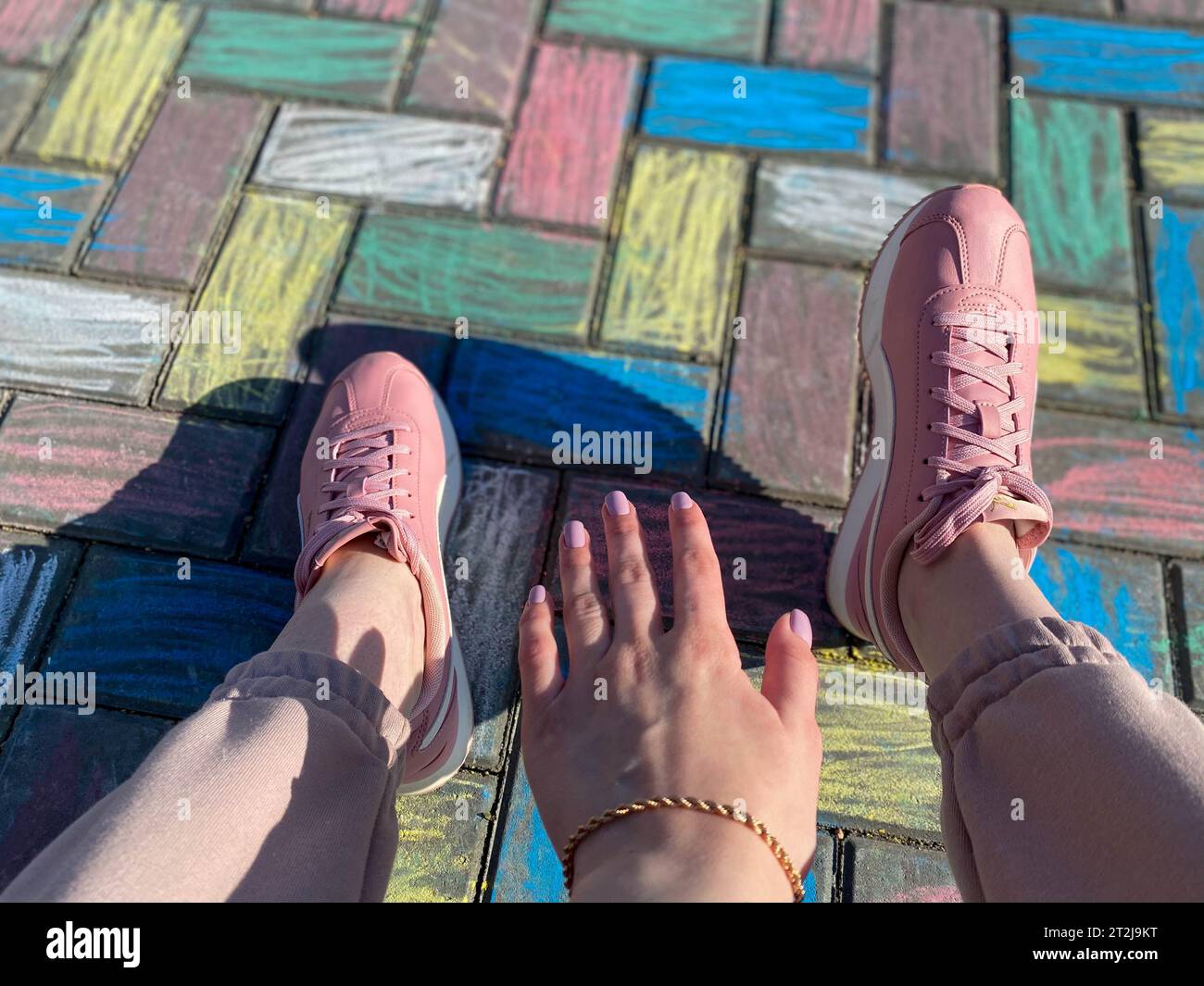 Beautiful female legs and hands in pink sneakers and fashionable pants ...
