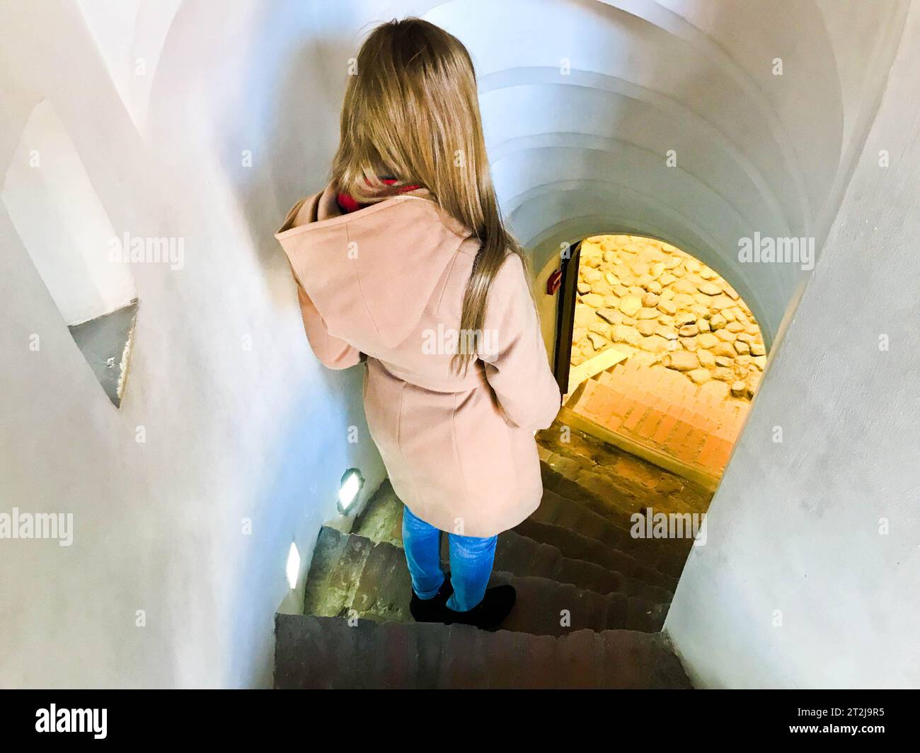 A girl, a woman descends the steep stone spiral stairs going down the ...