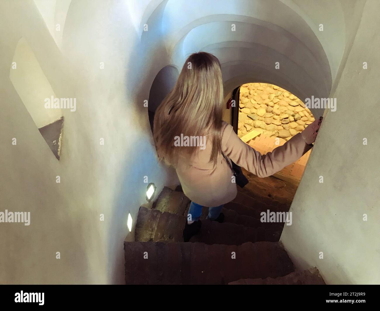 A girl, a woman descends the steep stone spiral stairs going down the ...