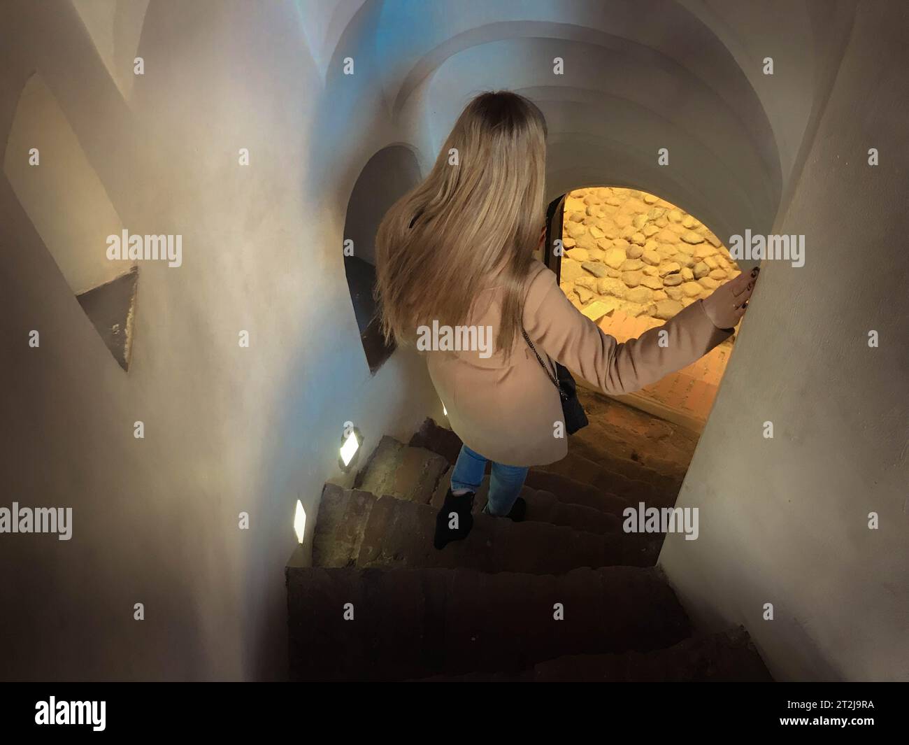 A girl, a woman descends the steep stone spiral stairs going down the ...