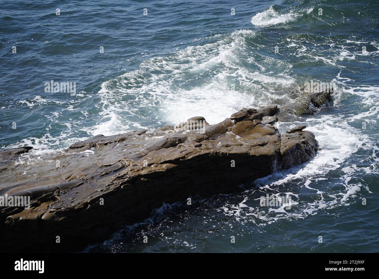 A large rock formation in the middle of an expansive body of blue water ...