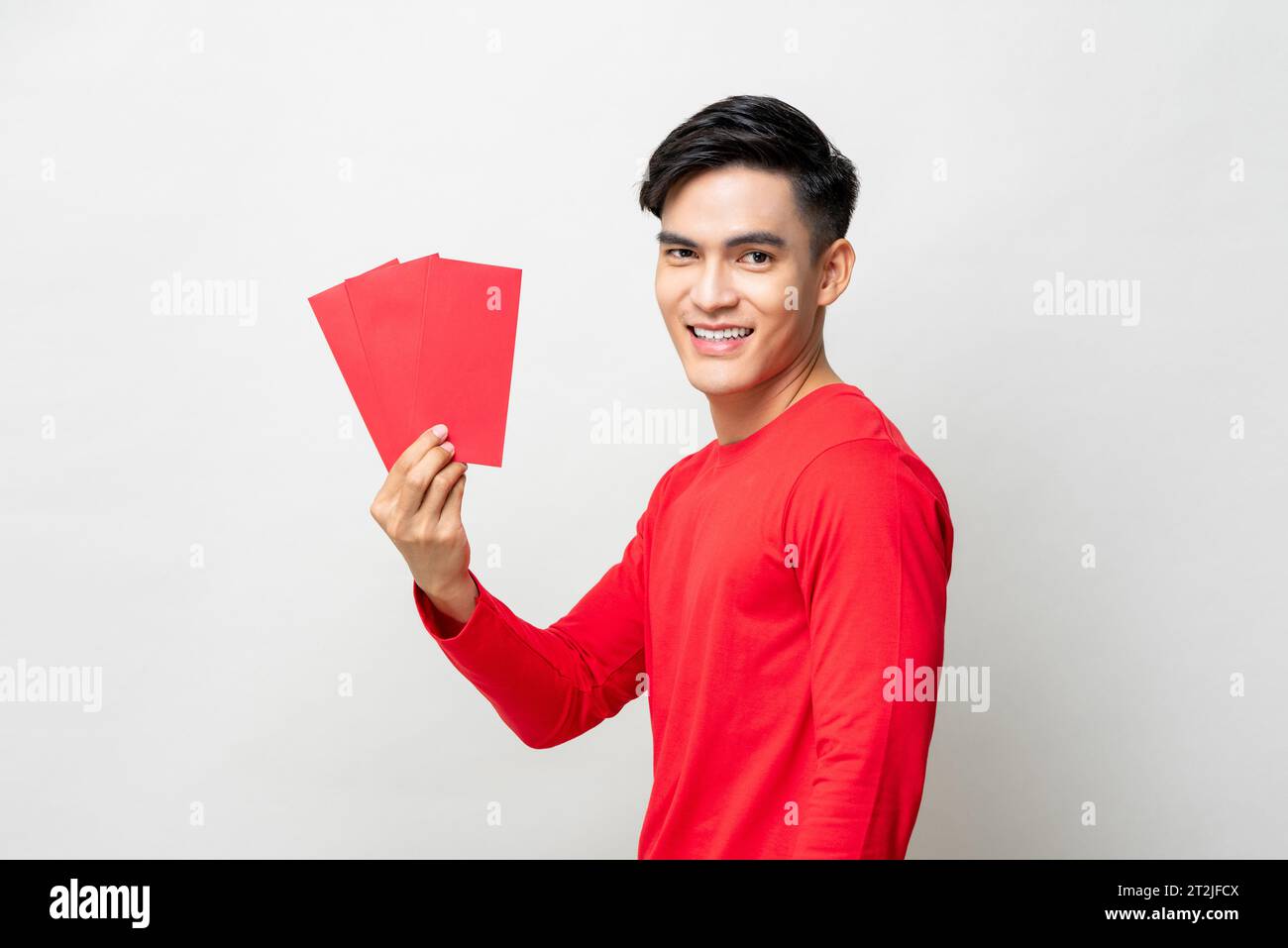 Smiling handsome Asian man holding red envelopes or Ang Pow in studio ...