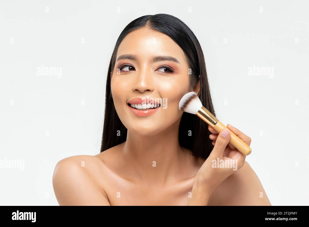 Merry young Asian woman smiling and looking away while applying powder ...