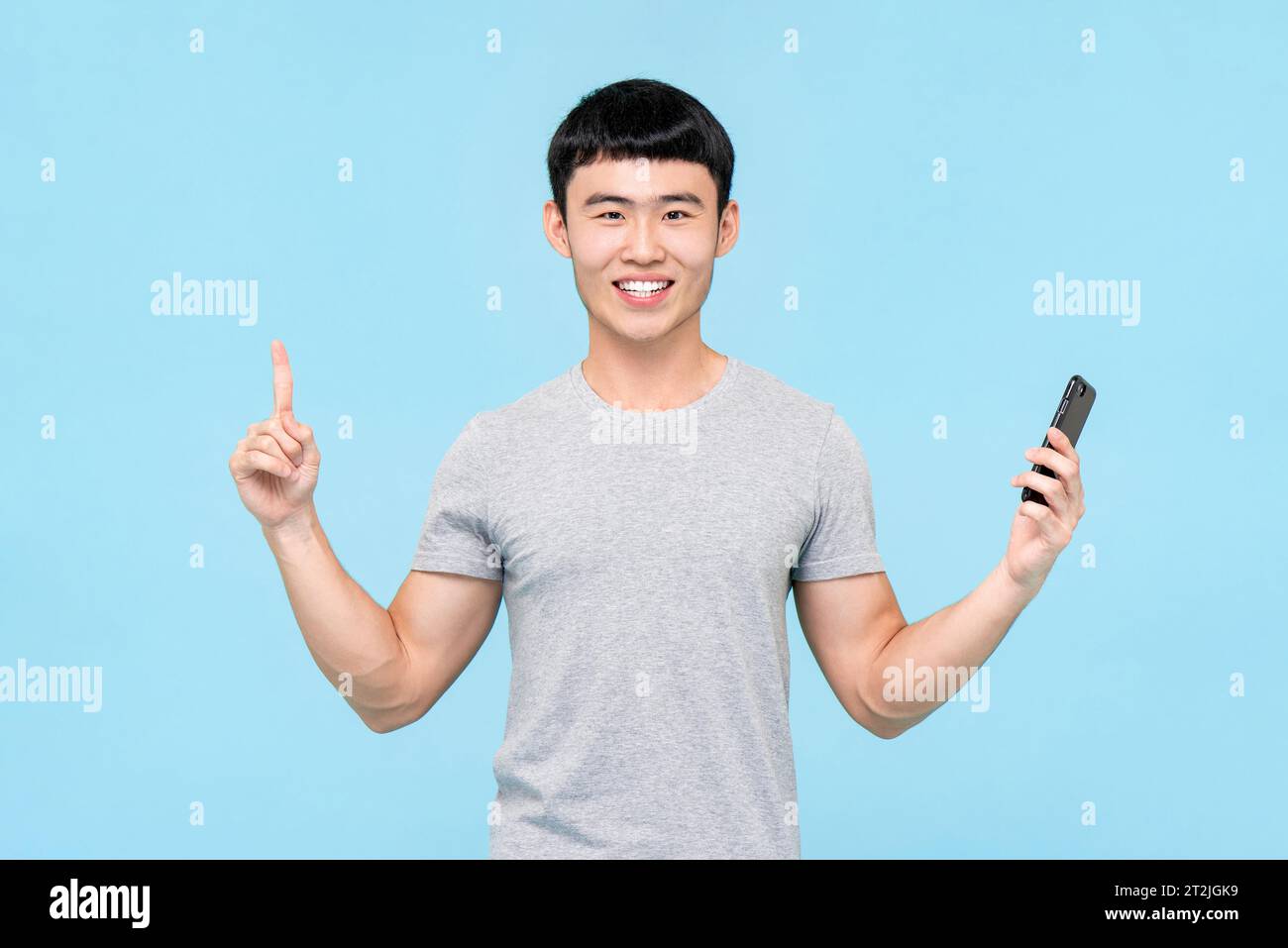 Positive Asian man in casual wear holding cellphone and pointing hand ...