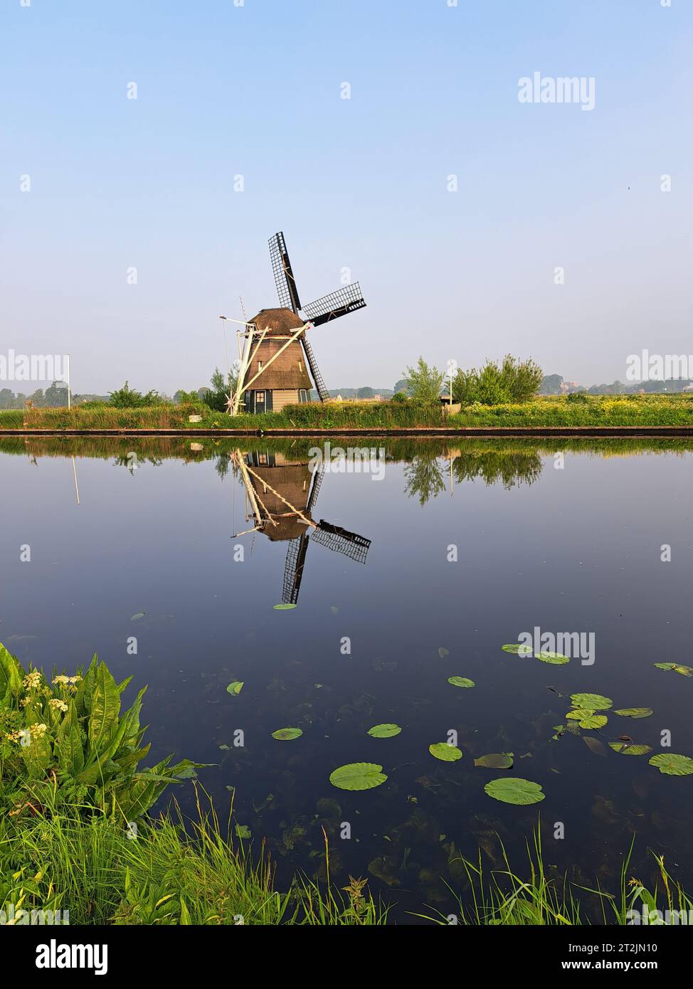 A tranquil scene of a small pond in front of an old-fashioned windmill ...