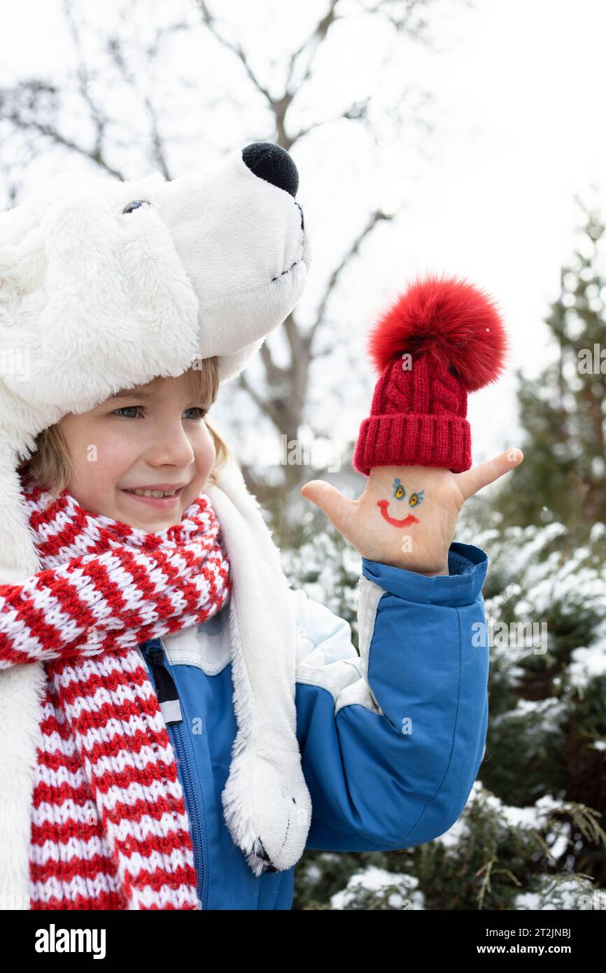 child is wrapped in striped red scarf and polar bear hat, smiling face ...