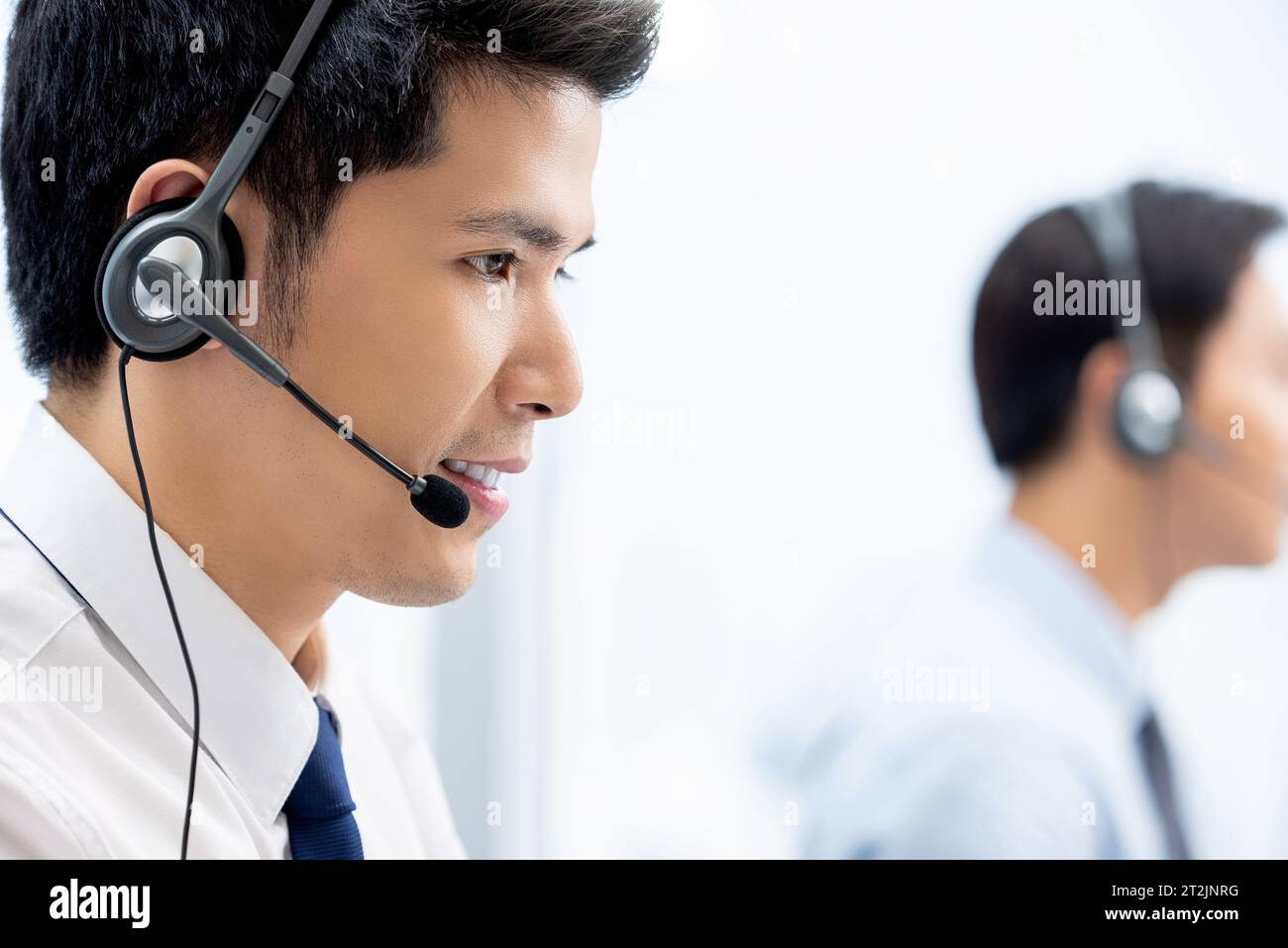 Side view of handsome Asian man operator in office wear and headset ...
